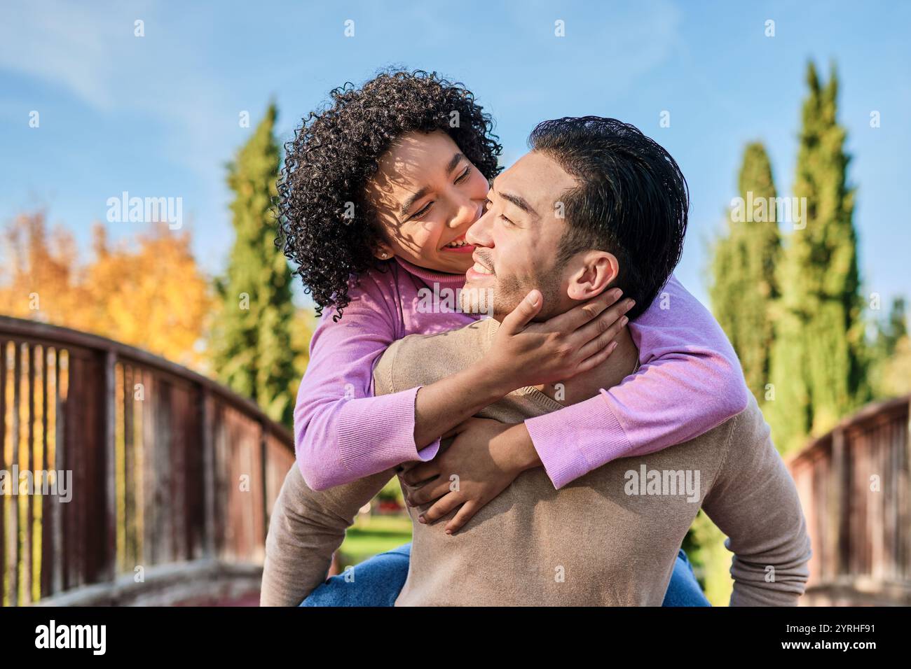 A joyful couple shares a playful piggyback ride on a scenic bridge ...