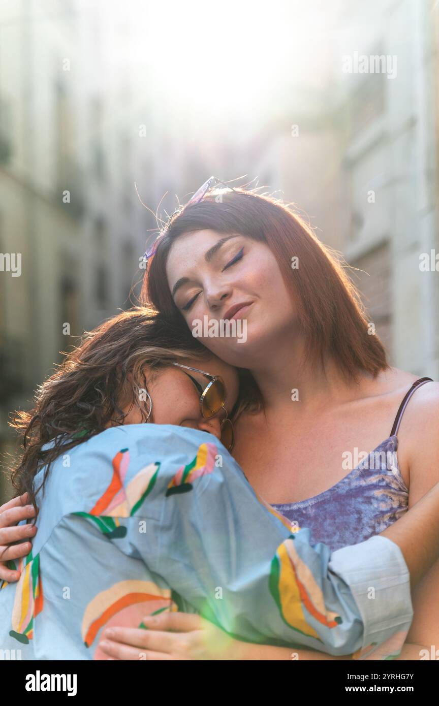 Two women share a tender embrace in a sunlit urban setting, one woman ...