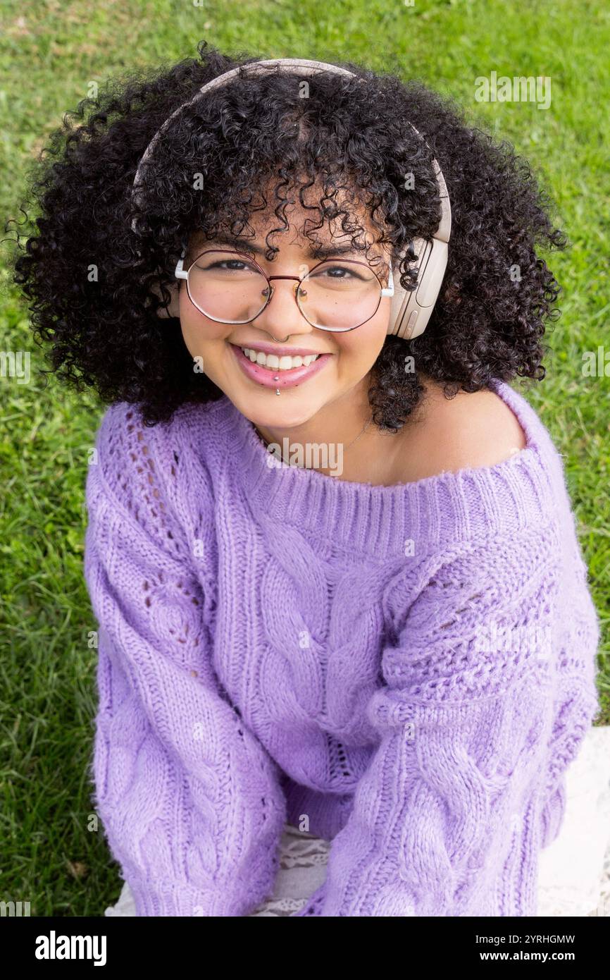 A cheerful Afro-Latino girl wearing glasses and headphones, sitting on ...