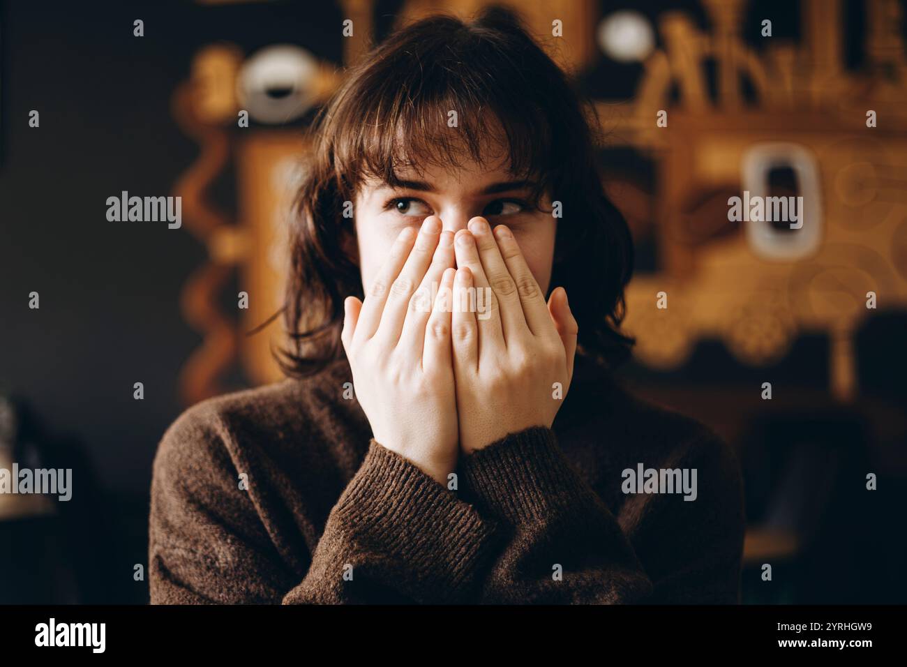 A young person with brown hair covering their face with their hands ...