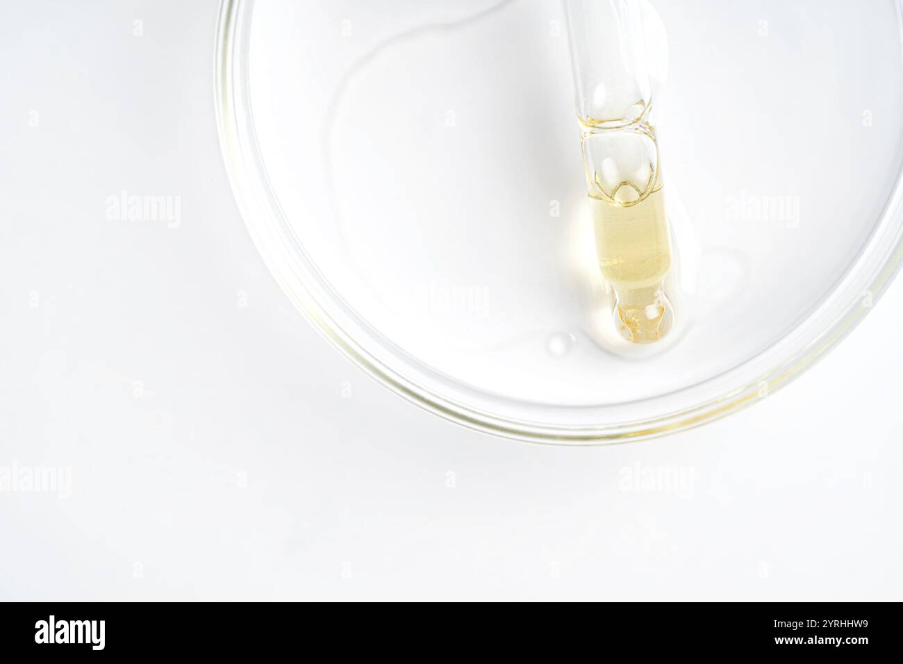 A glass pipette holds a viscous liquid in a petri dish against a clean ...
