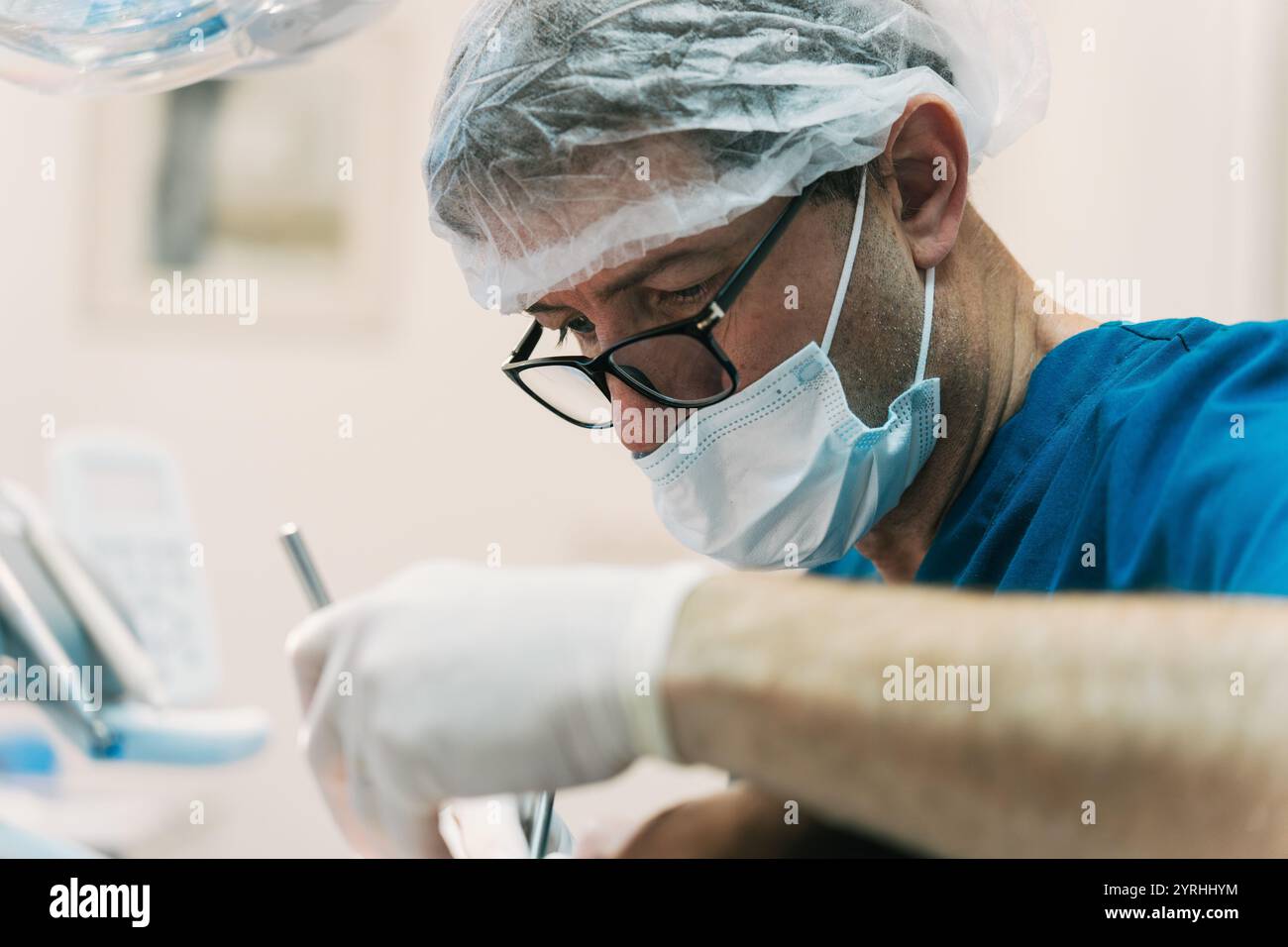 A focused dental professional in surgical attire and safety gear ...