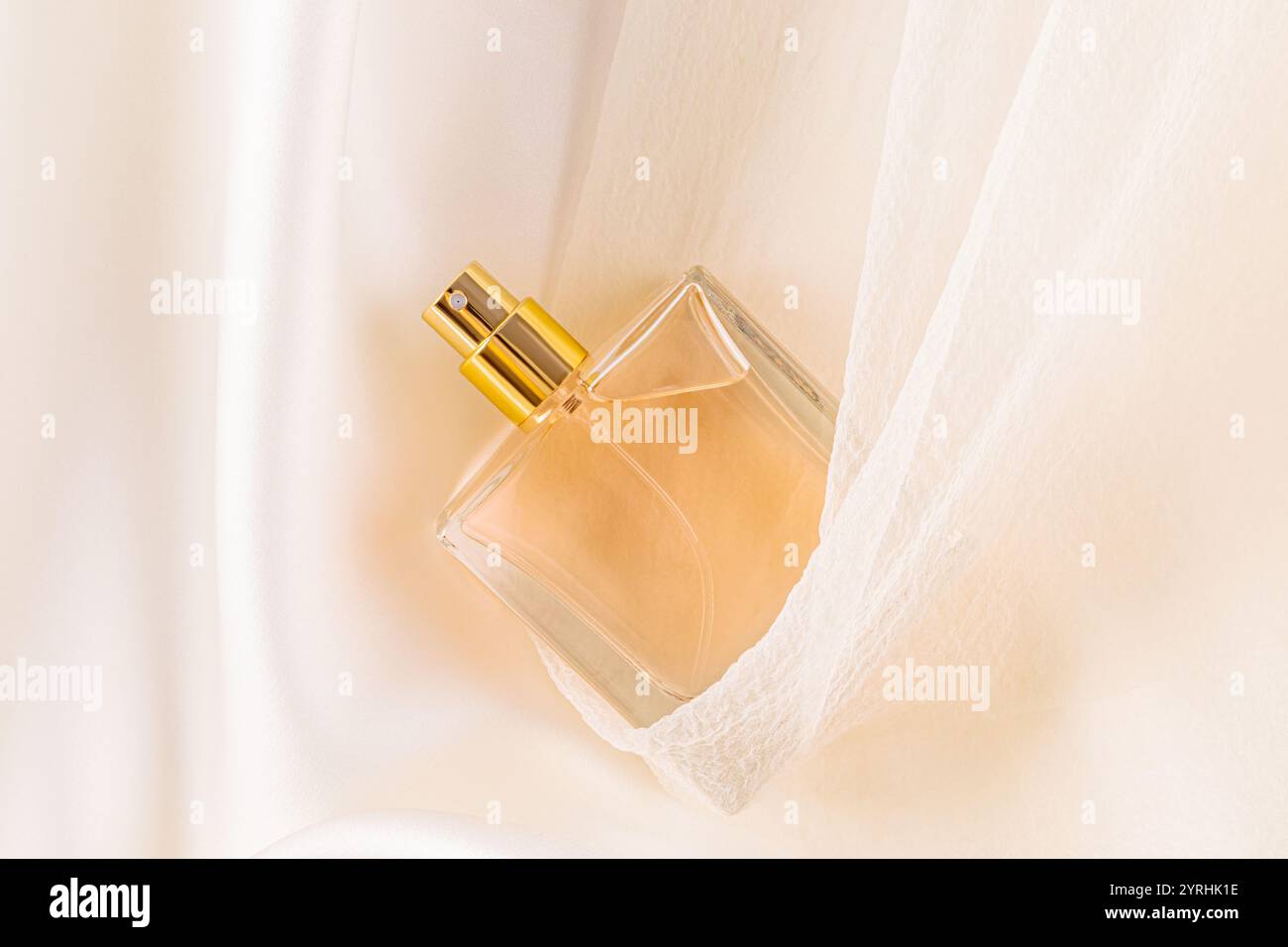 A delicate glass perfume bottle with golden accents lies on soft, cream ...