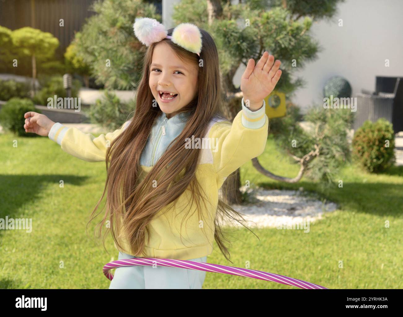 A joyful child in a yellow outfit plays with a hula hoop in a sunny ...