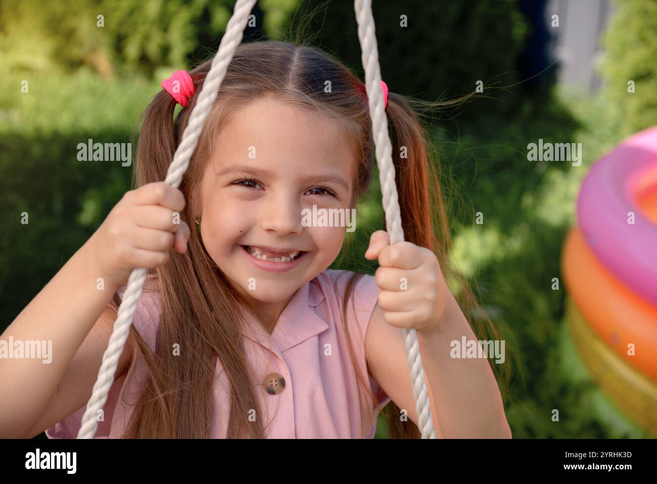 A cheerful child with pigtails smiles brightly while holding onto a ...