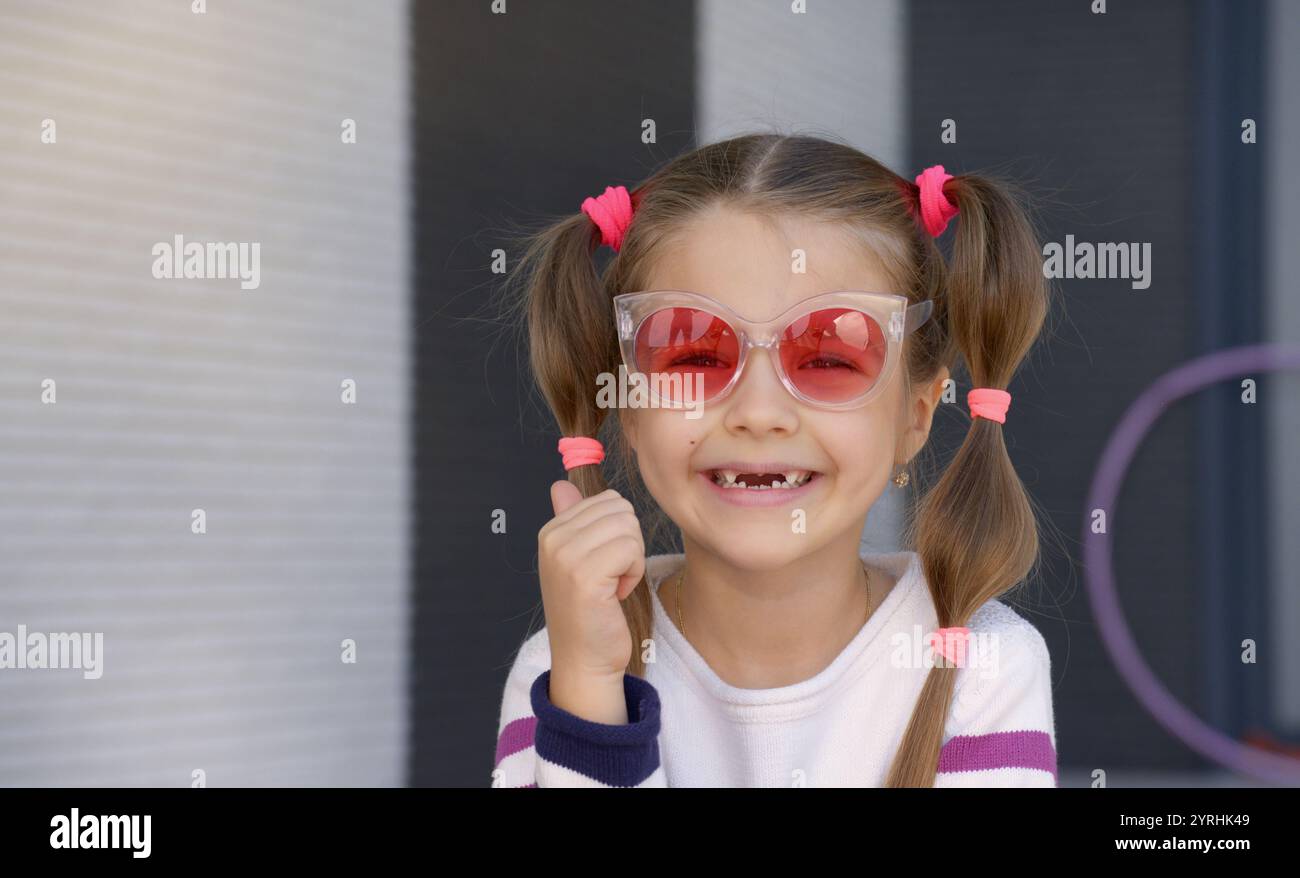 A joyful child with pigtails and sunglasses beams with a toothy grin at ...