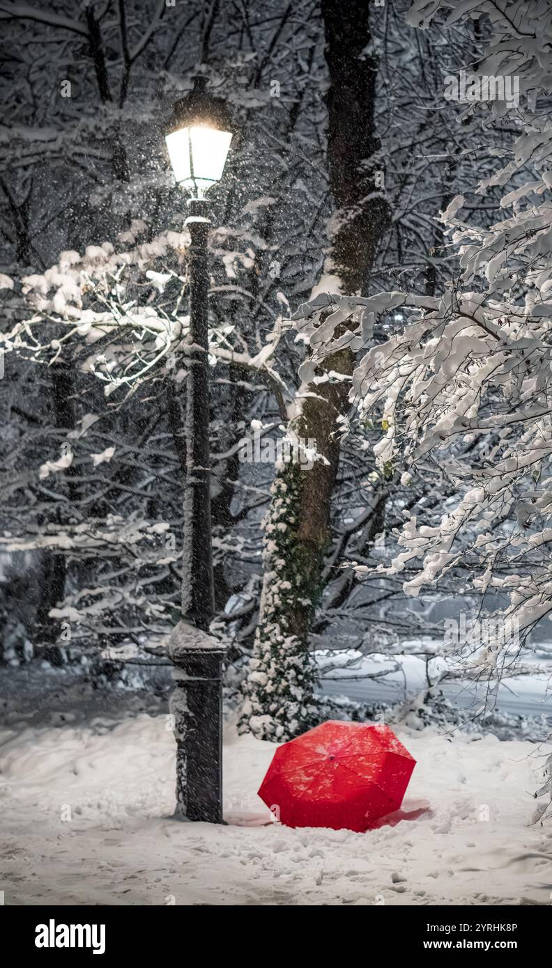 A vibrant red umbrella sits under a glowing streetlamp during a snowy ...