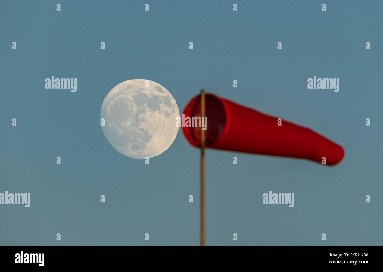 A bright full moon rises against a clear blue sky at dusk, juxtaposed ...