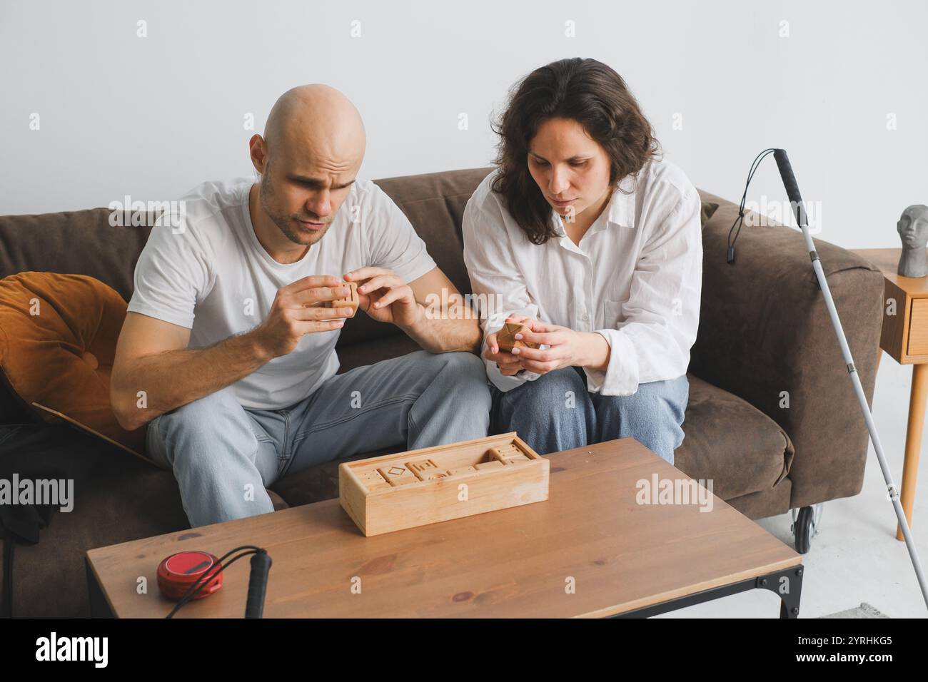 A blind couple sits on a sofa, deeply engaged in solving tactile ...
