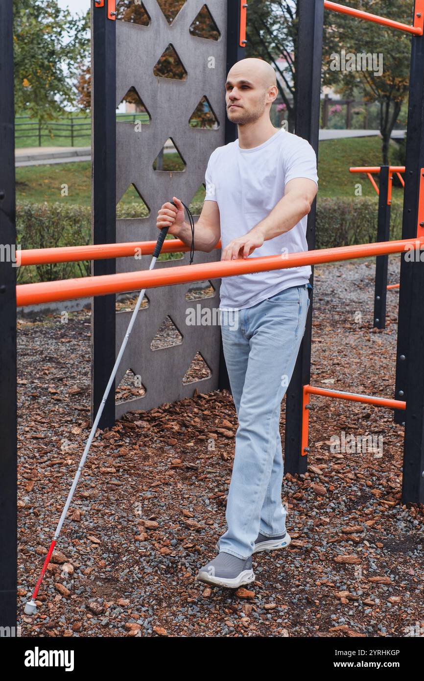A visually impaired blind man uses a white cane to navigate an outdoor ...