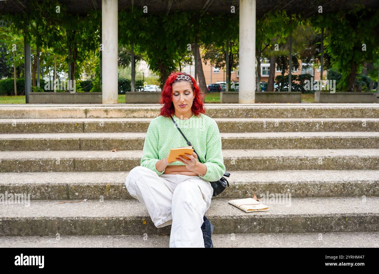 A trans woman with red hair and a green sweater reads a book while ...