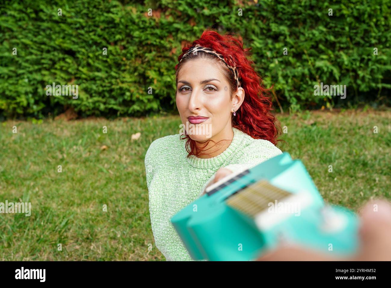 A trans woman with vibrant red hair and a mint sweater holds a teal ...