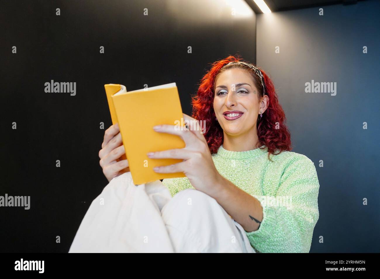A trans woman with red hair relaxes while reading a book Her joyful ...