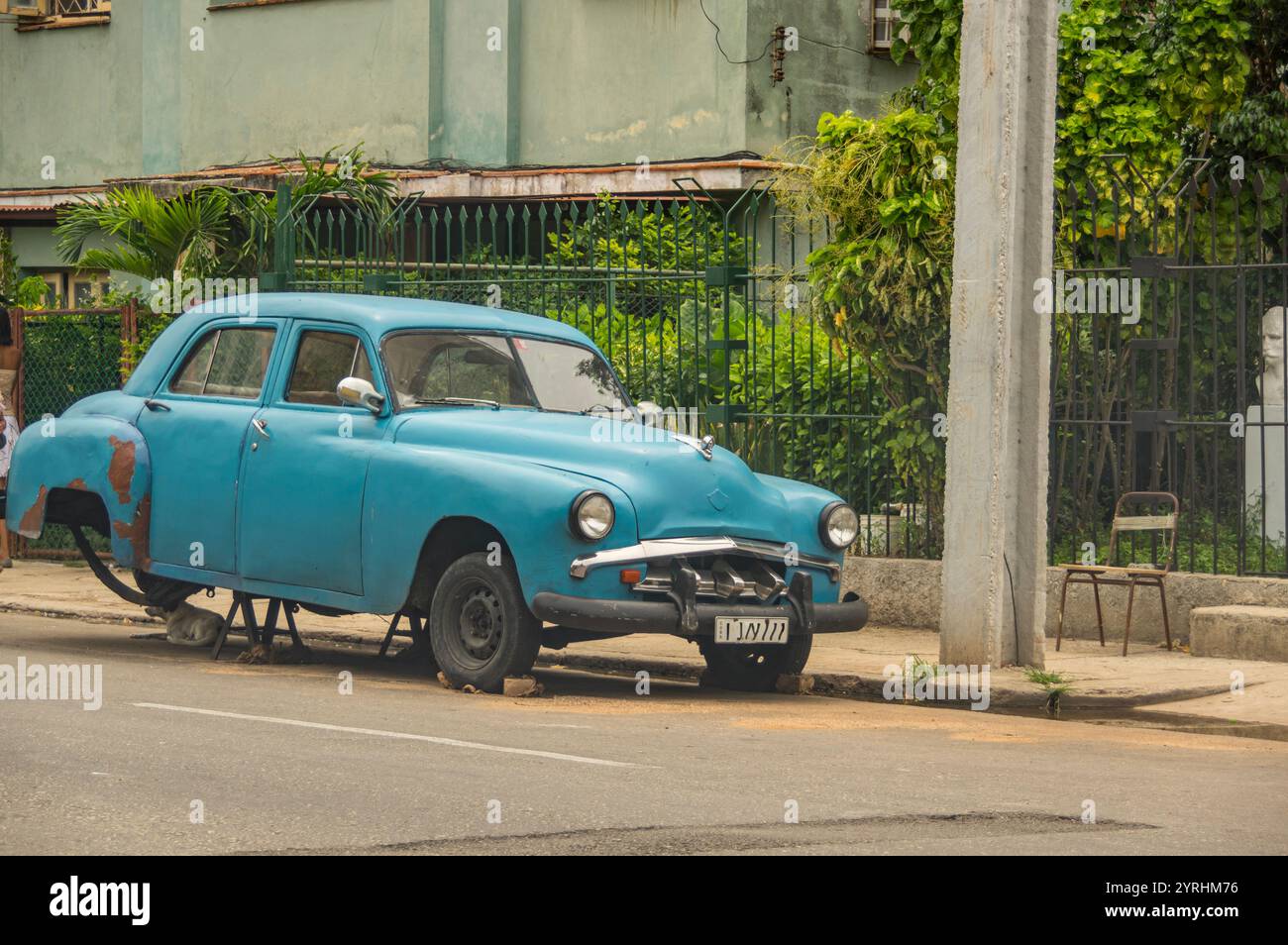 A vintage blue car is parked on a street with one wheel missing The vehicle shows rust, while a ...