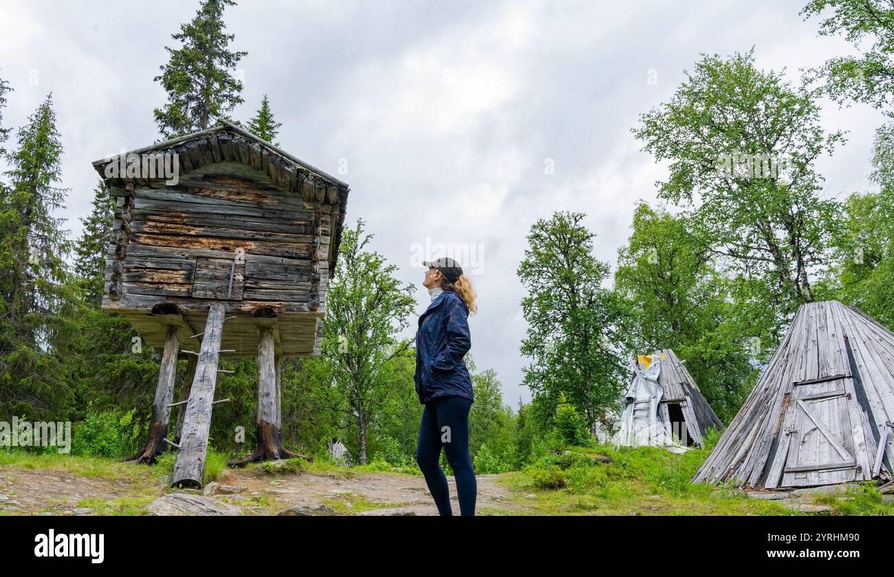 A woman admires traditional Sami structures in the lush wilderness of ...