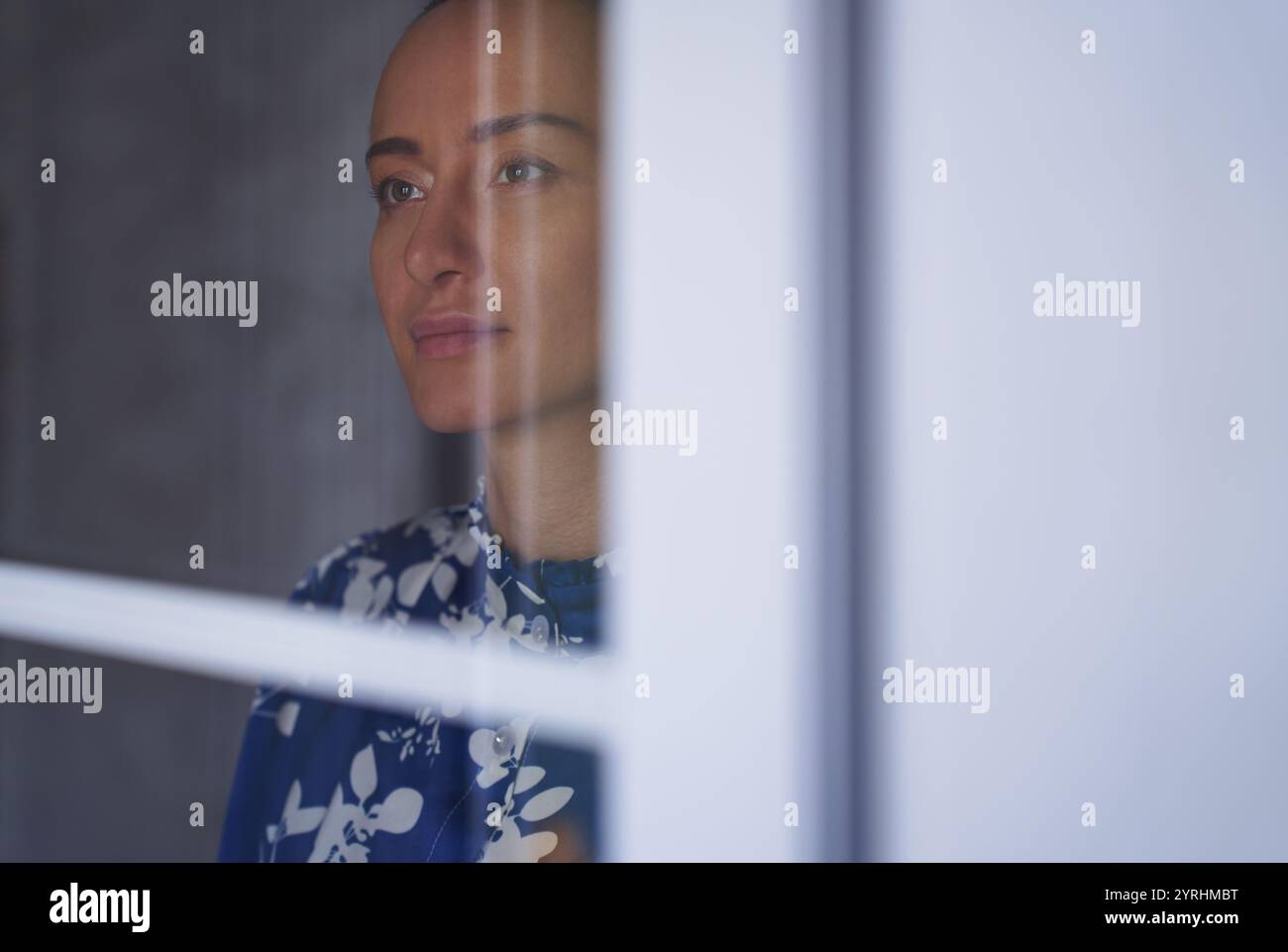 A woman gazes thoughtfully outside, framed by a window. Her serene ...