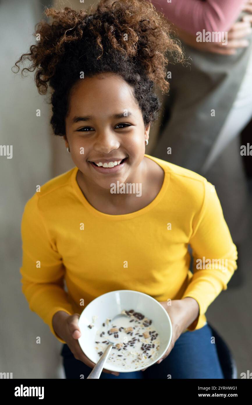 Happy african american child girl having breakfast eating cereal in ...