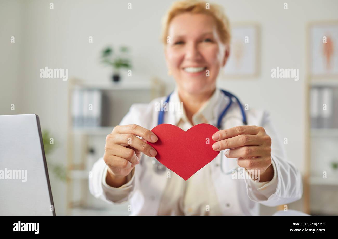 Female smiling doctor showing red heart paper symbol, cardiologist ...