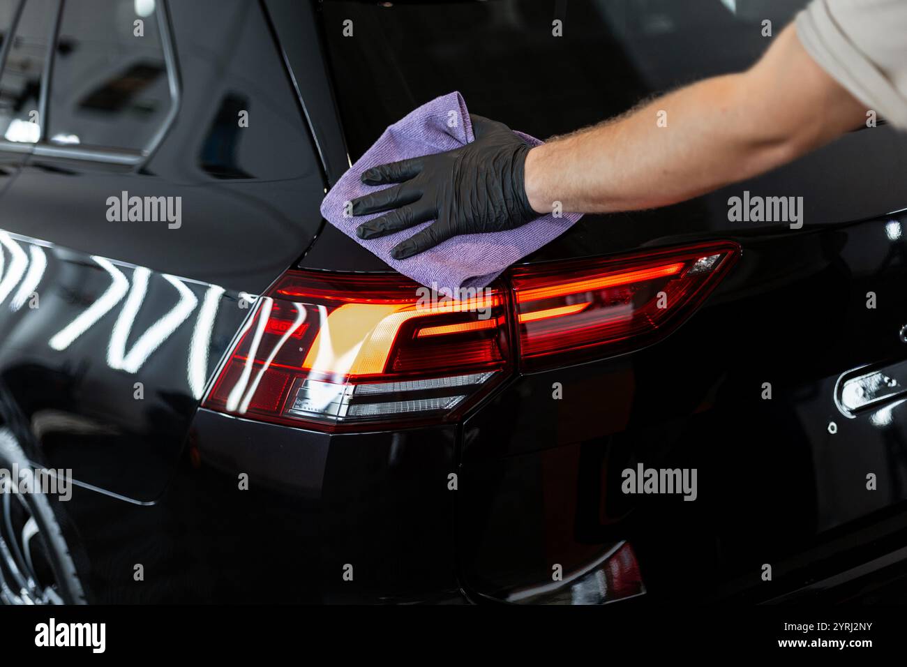 Man wipes a car dry with a rag. Black car with taillight in garage ...