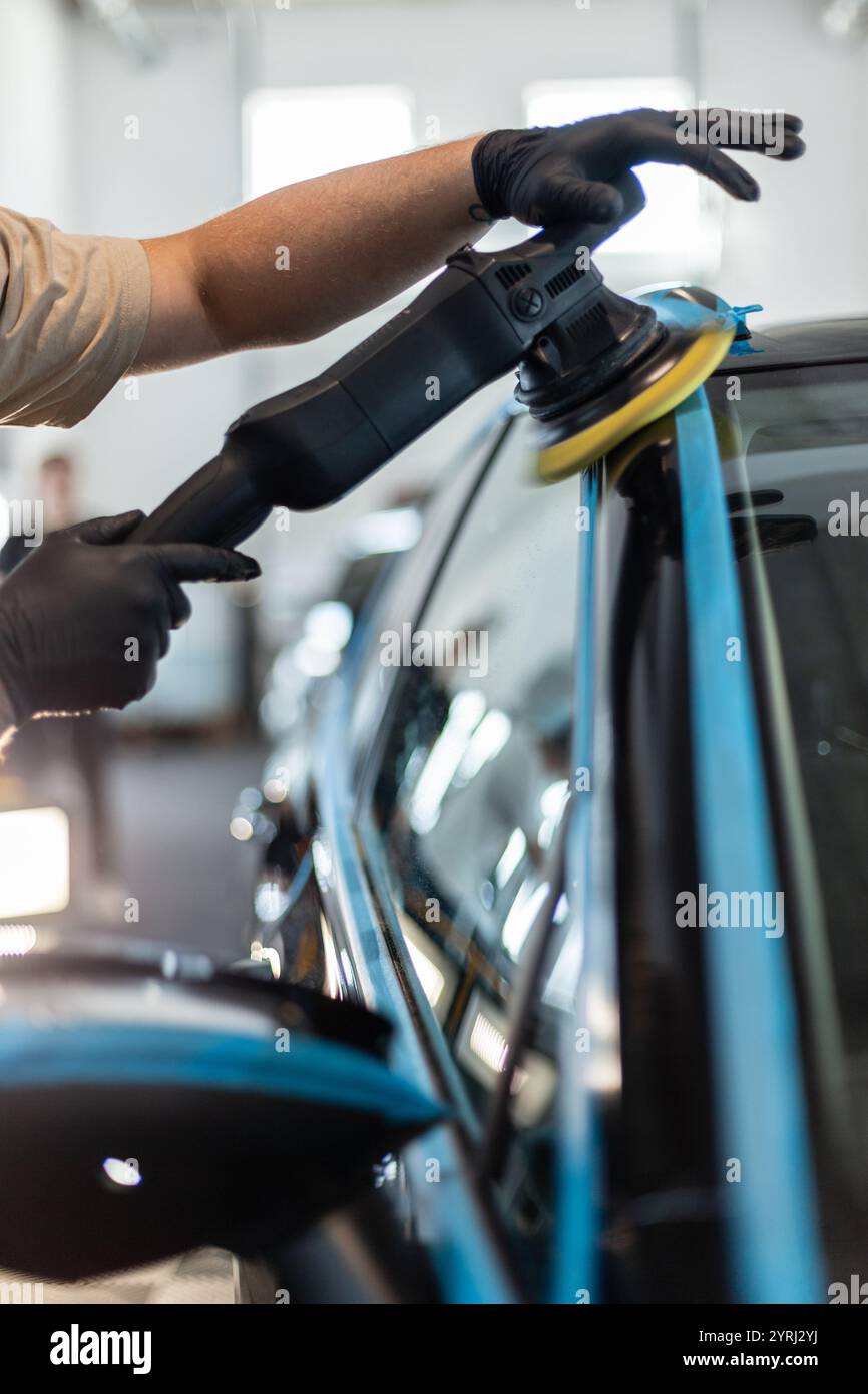 Professional man with polishing tool polishing black car in detailing ...