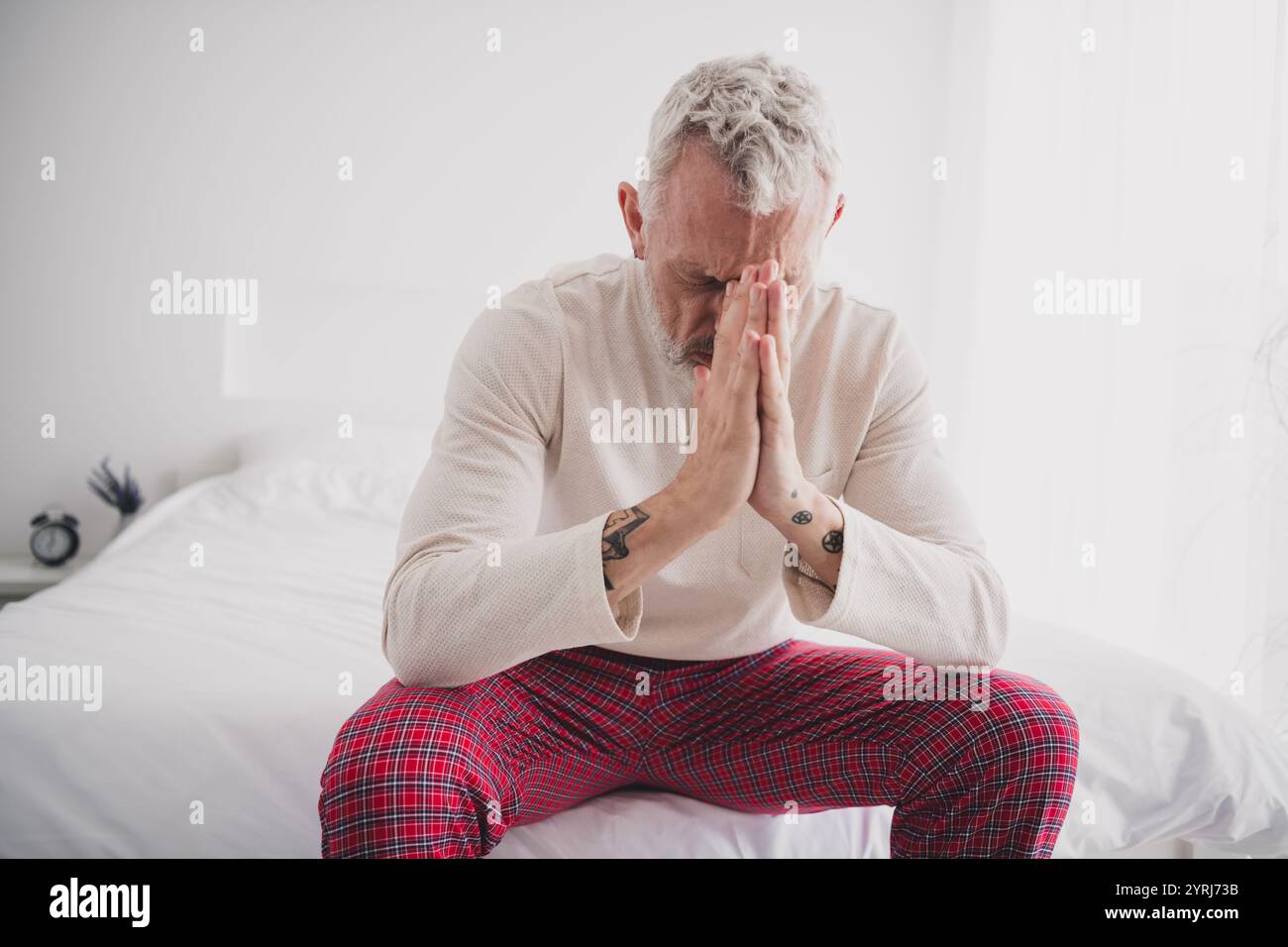 Mature man sitting on bed in morning light, wearing pajamas, lost in ...