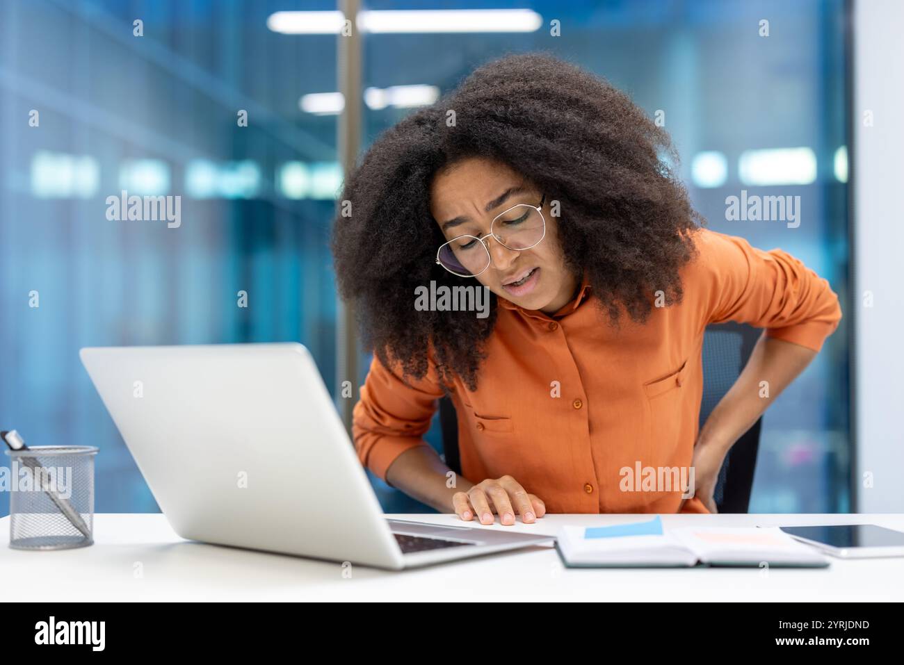 Young businesswoman feeling discomfort due to back pain at her desk ...