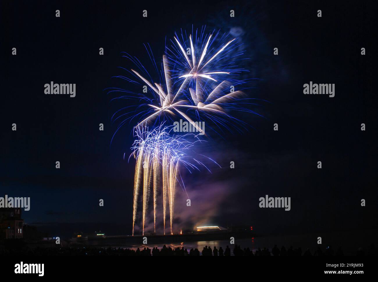 Silhouettes of people watching the firework display over the sea. Blue ...