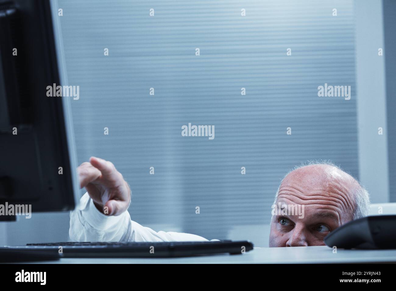 Mature businessman hiding behind his desk, pointing at the computer ...