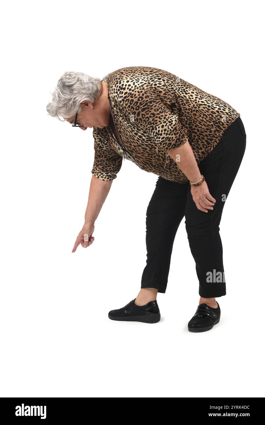 senior woman crouching and pointing finger at the ground on white ...