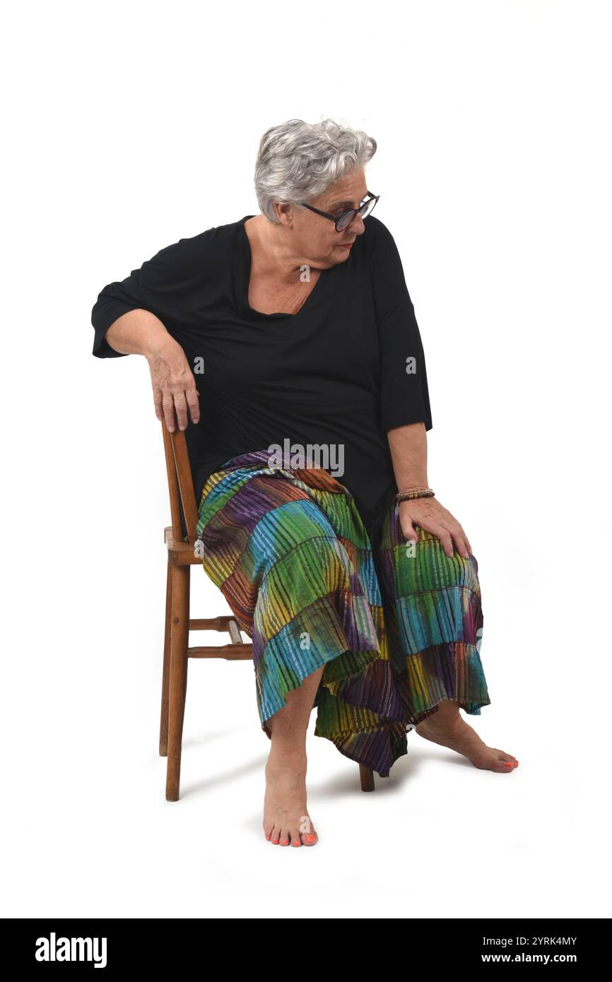 front view of senior woman sitting on chair, barefoot, look away on ...