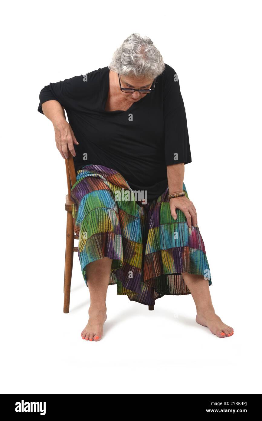 front view of senior woman sitting on chair, barefoot, look down on ...