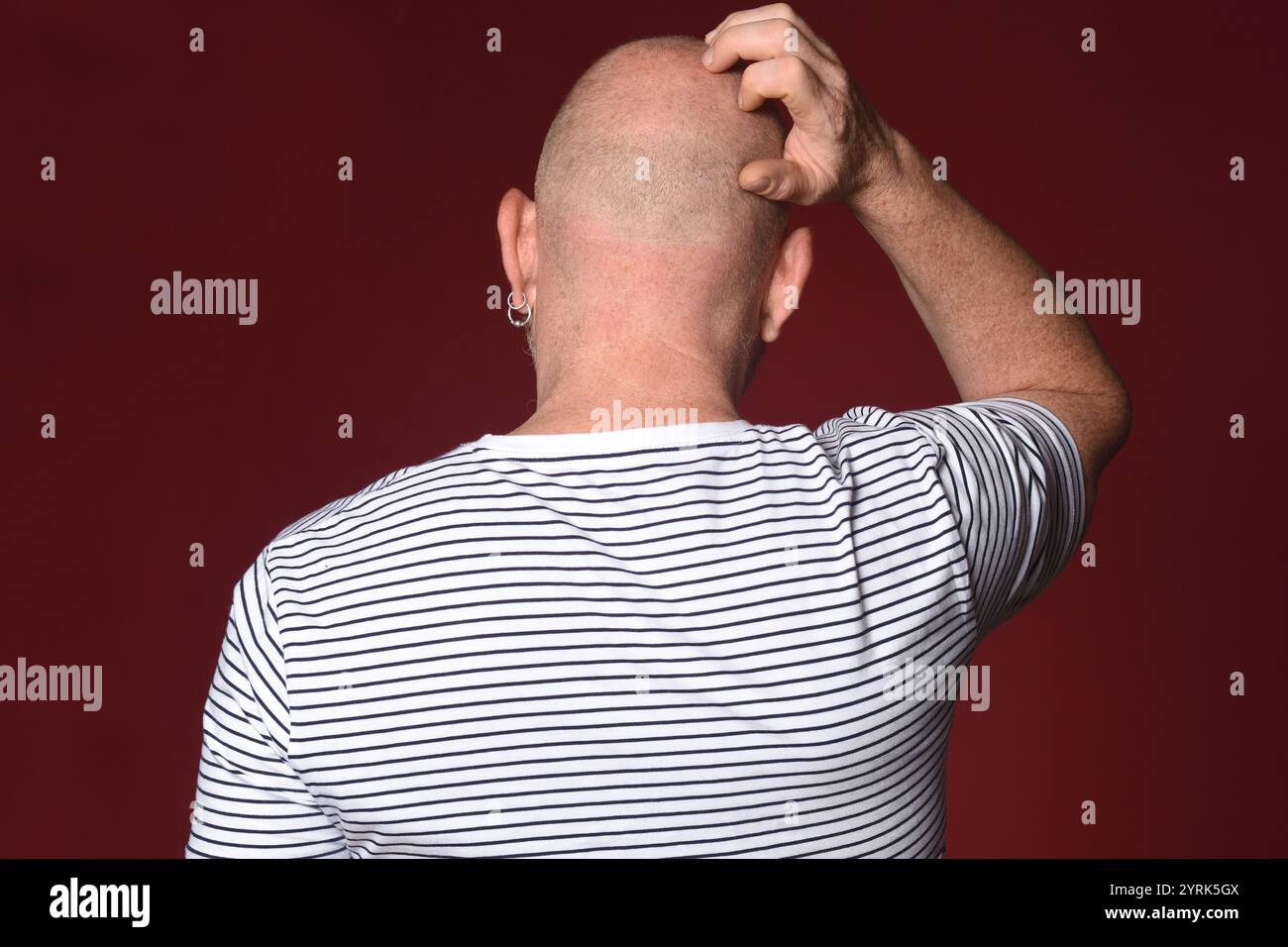 Rear view of a man touching his head with his hand on a red background ...