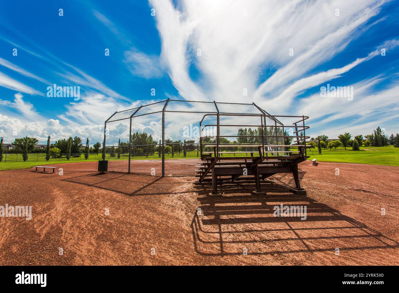 A baseball field with a dugout and a bench. The bench is empty. The sky ...