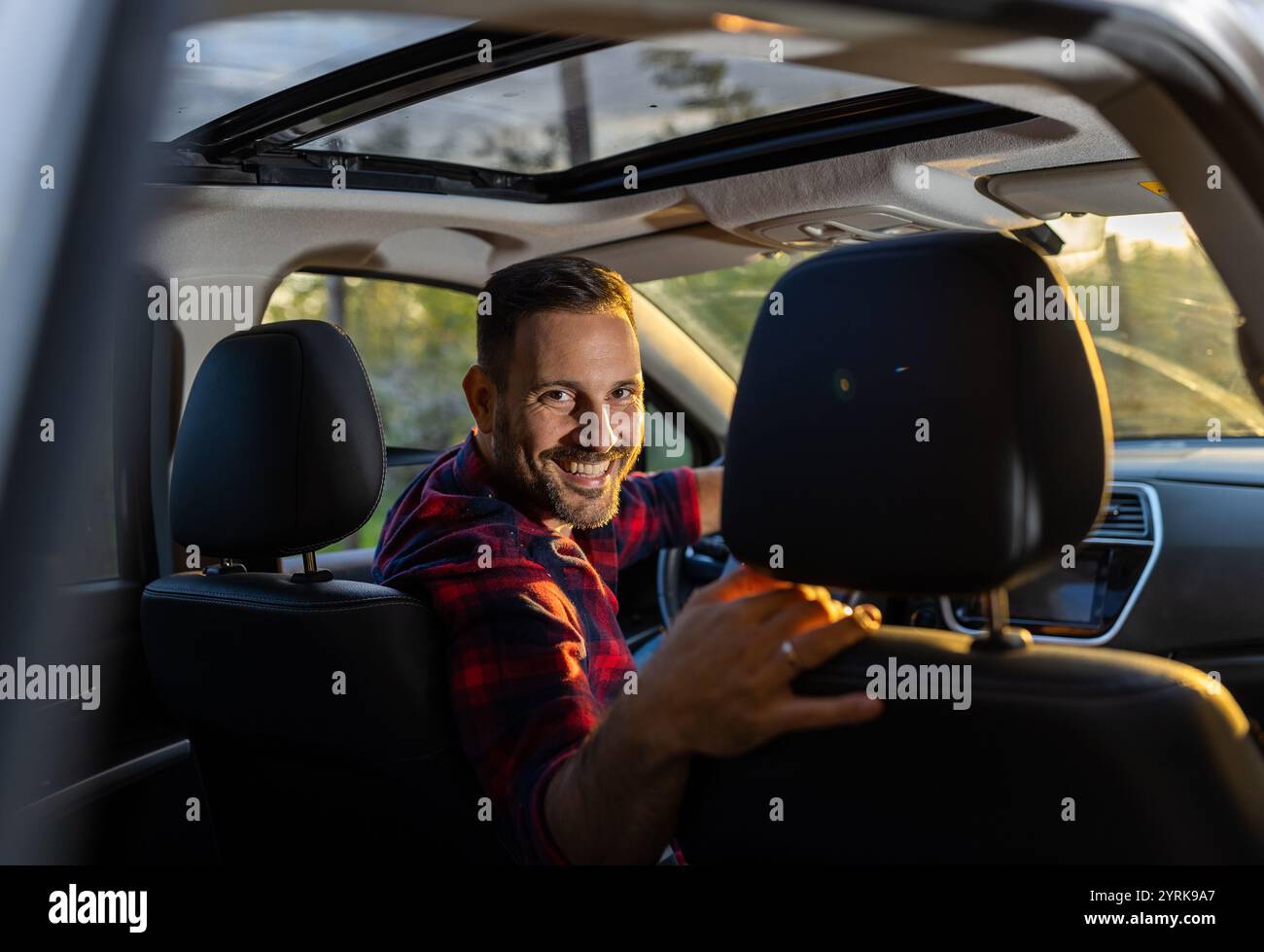 Handsome smiling man driving car and looking over shoulder at back ...