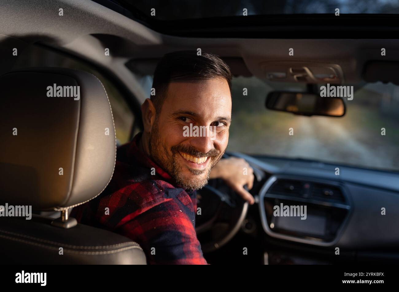 Handsome smiling man driving car and looking over shoulder at back ...
