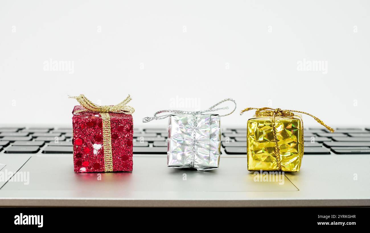 Three tiny gift boxes in red, silver, and gold sit atop a laptop ...