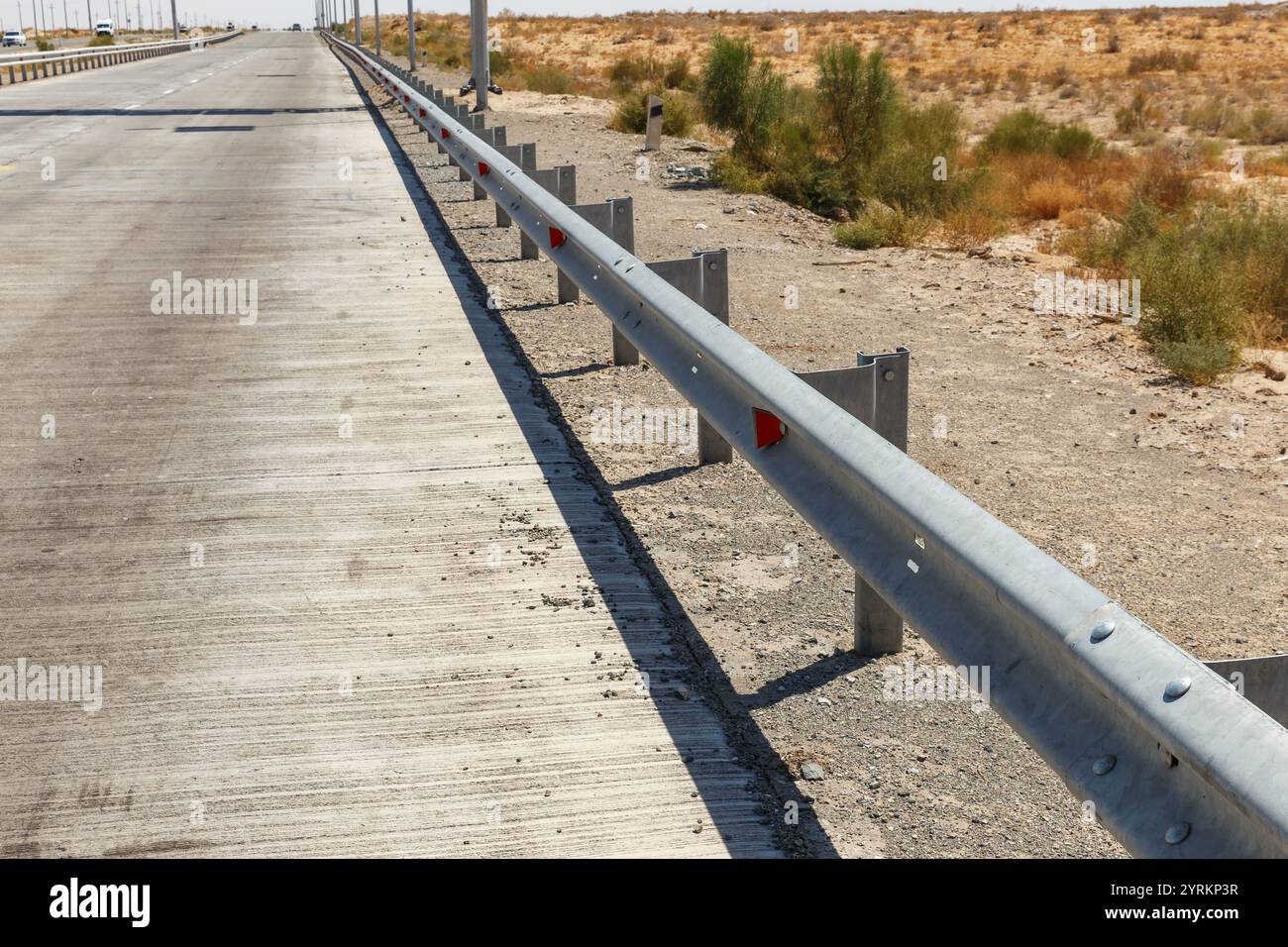 Fencing lines the side of a long road with concrete pavement ...