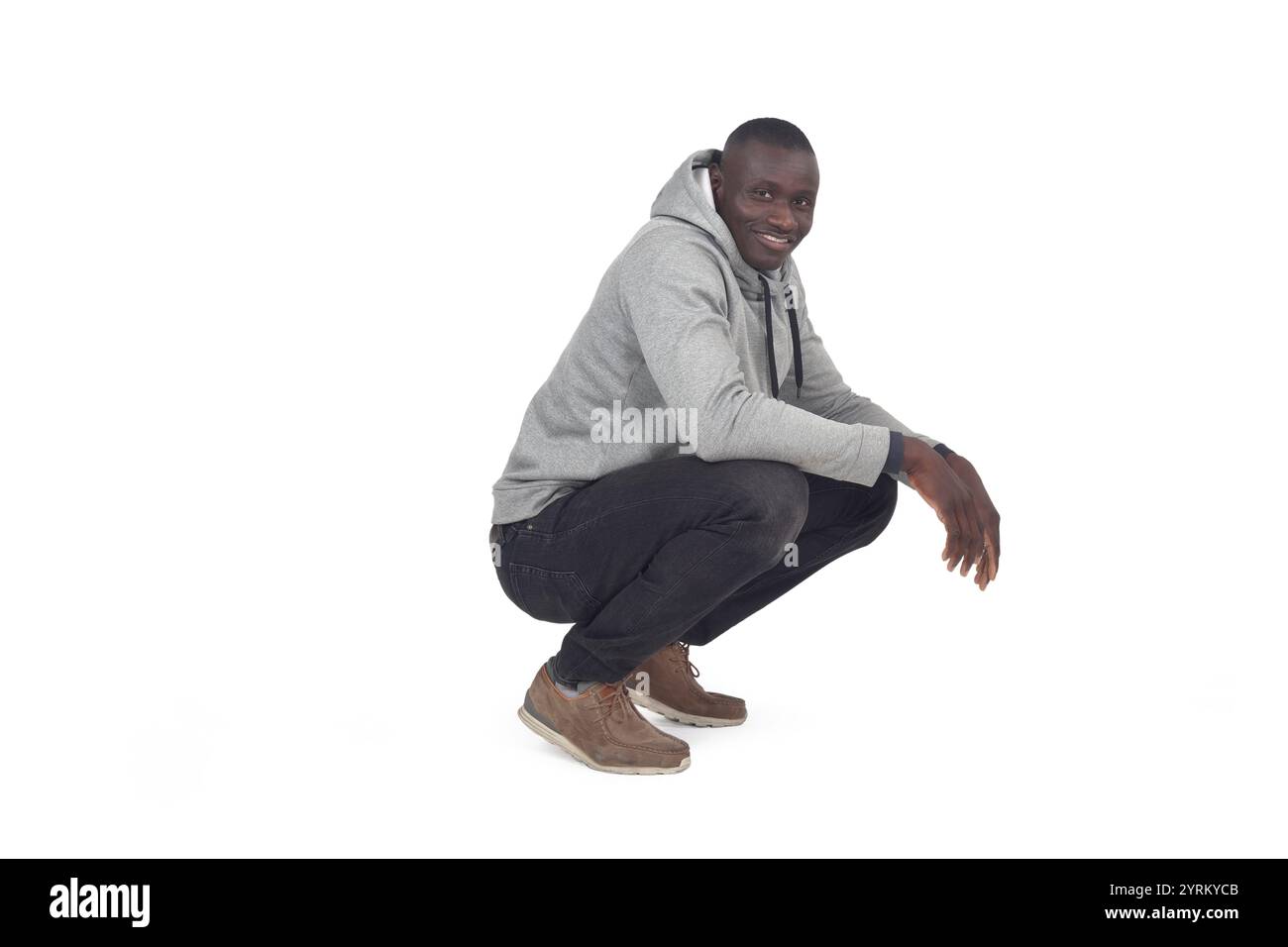 side view of man squatting and looking at camera on white background ...