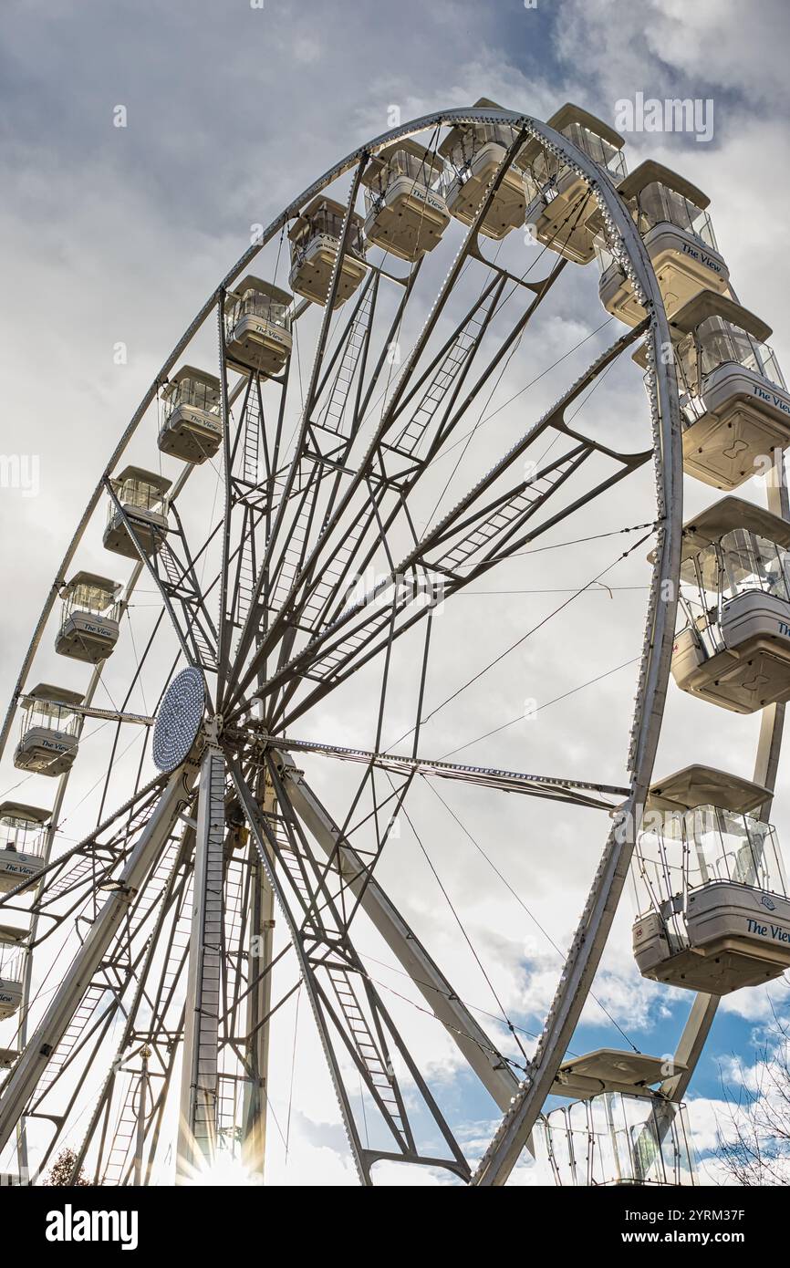 A low-angle view of a Ferris wheel against a cloudy sky. The wheel is ...