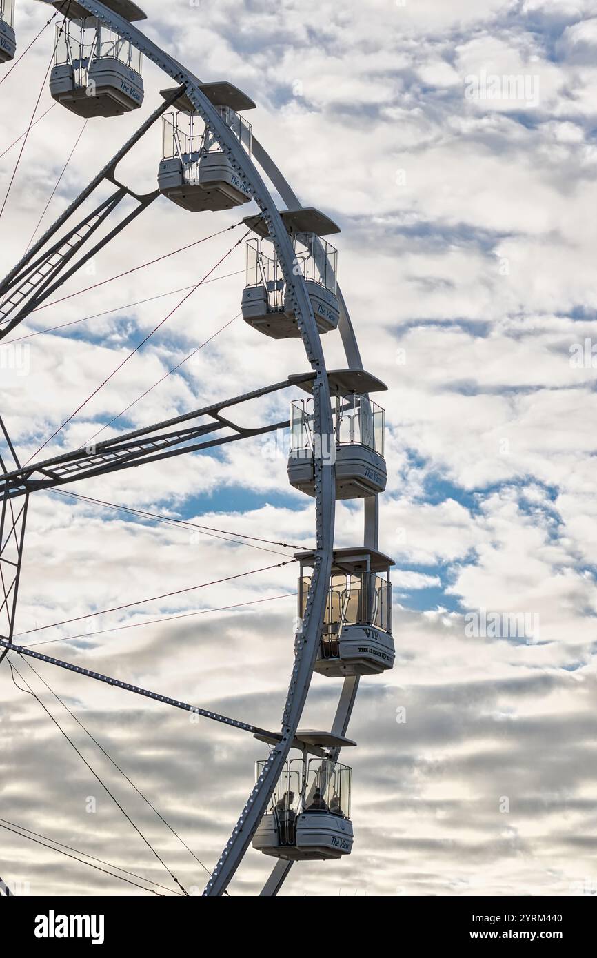 Partial view of a Ferris wheel against a cloudy sky. Several passenger ...