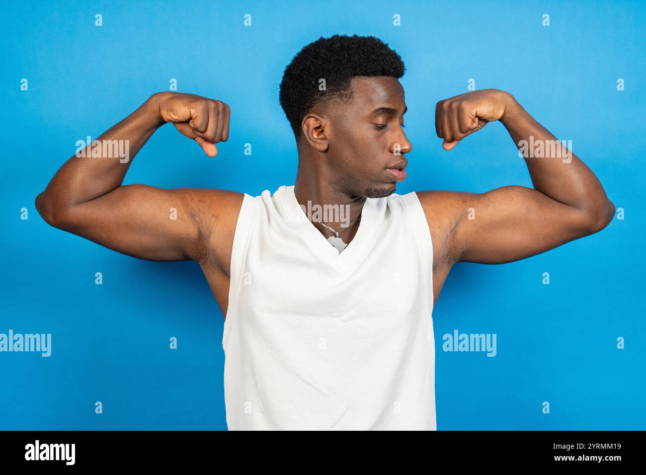 Strong sportsman flexing biceps while standing against blue backdrop ...