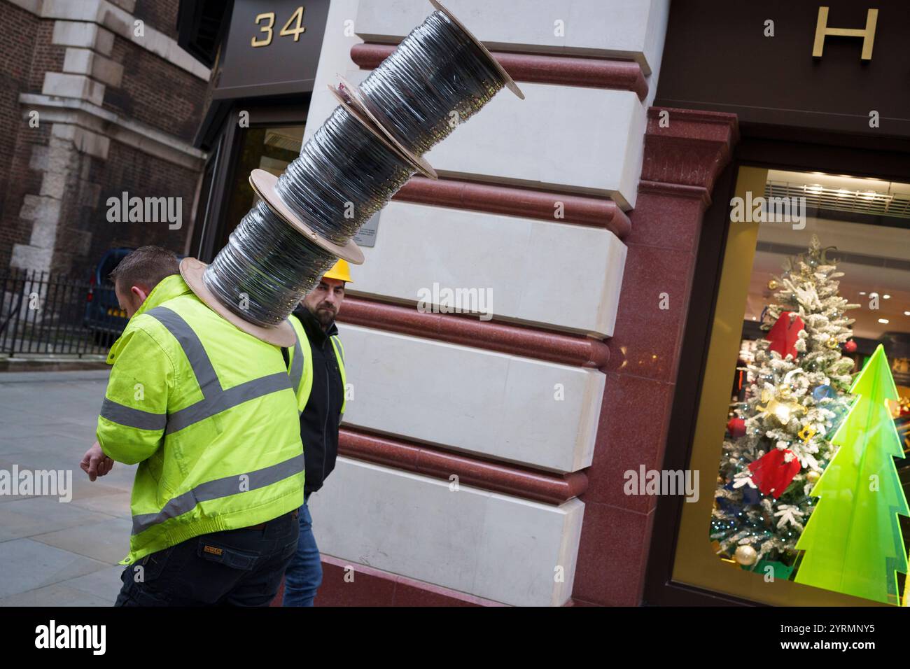 A workman carries a heavy load of electrical wiring coils, on Jermyn ...