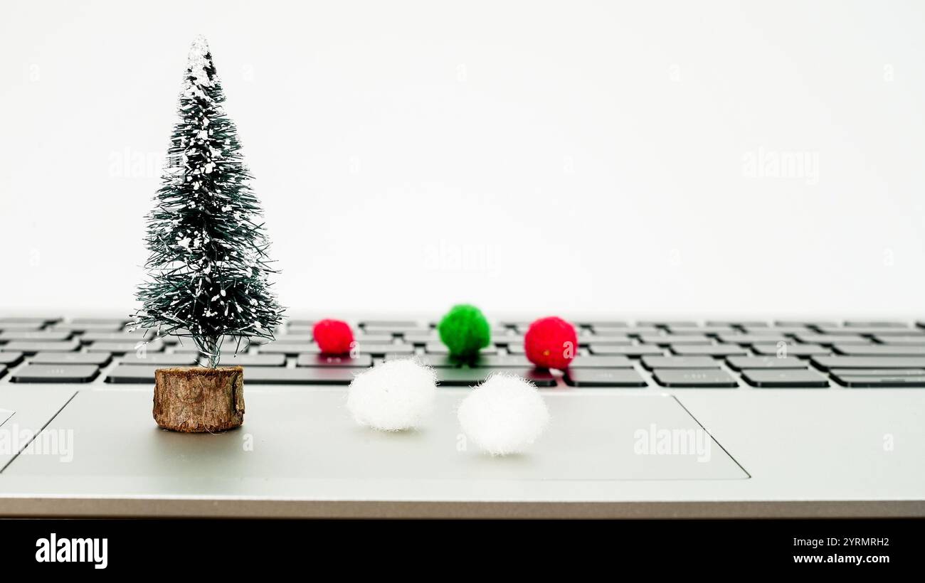 A tiny Christmas tree sits on a laptop keyboard alongside colorful pom ...