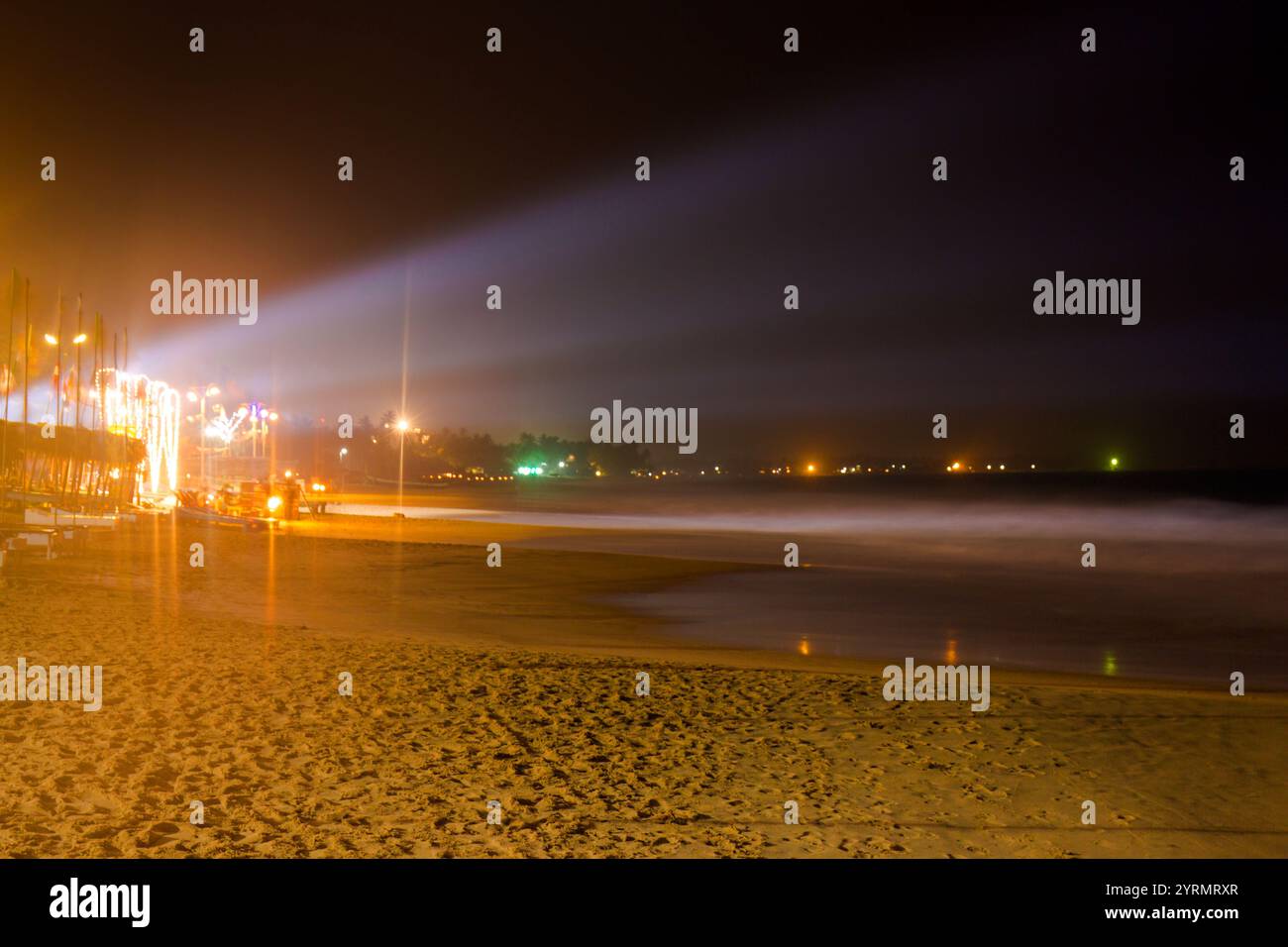 A beach at night with lights on the buildings and the water. The beach ...
