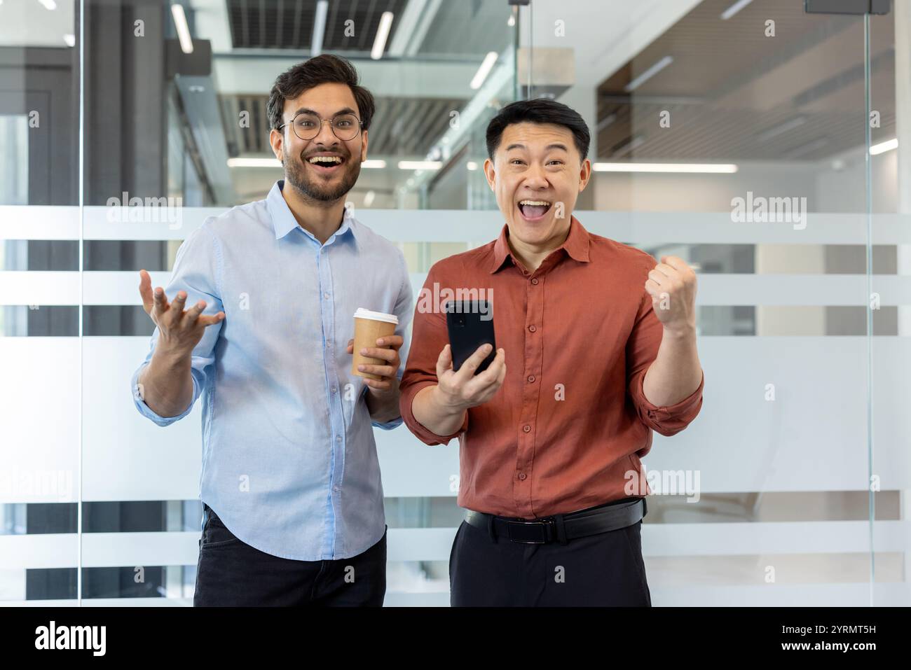 Two smiling colleagues celebrate a success looking at a smartphone in ...