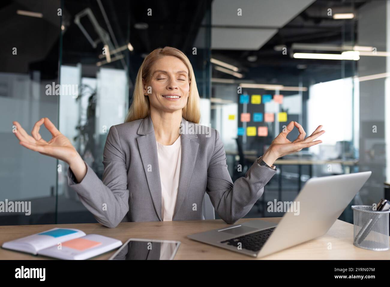 Mature businesswoman practicing meditation at her desk in a modern ...