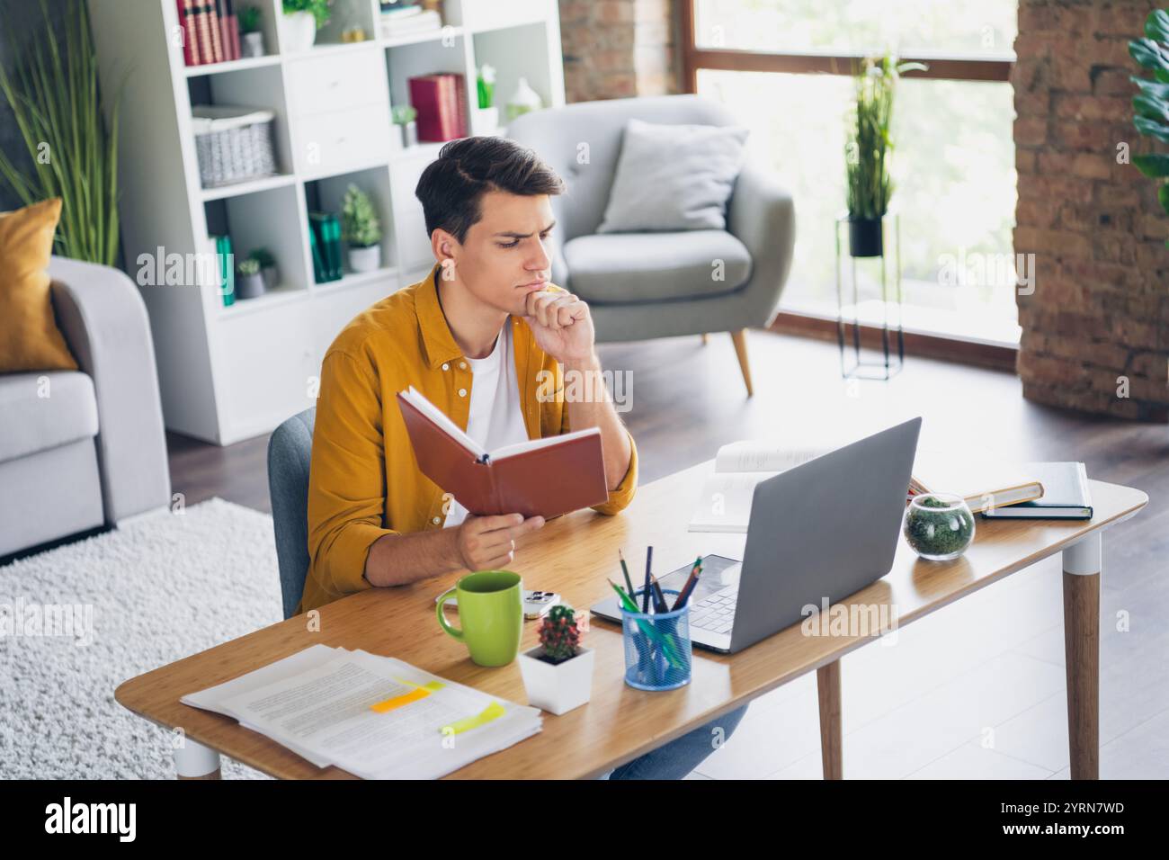 Attractive young man studying at home with laptop and books in a cozy ...