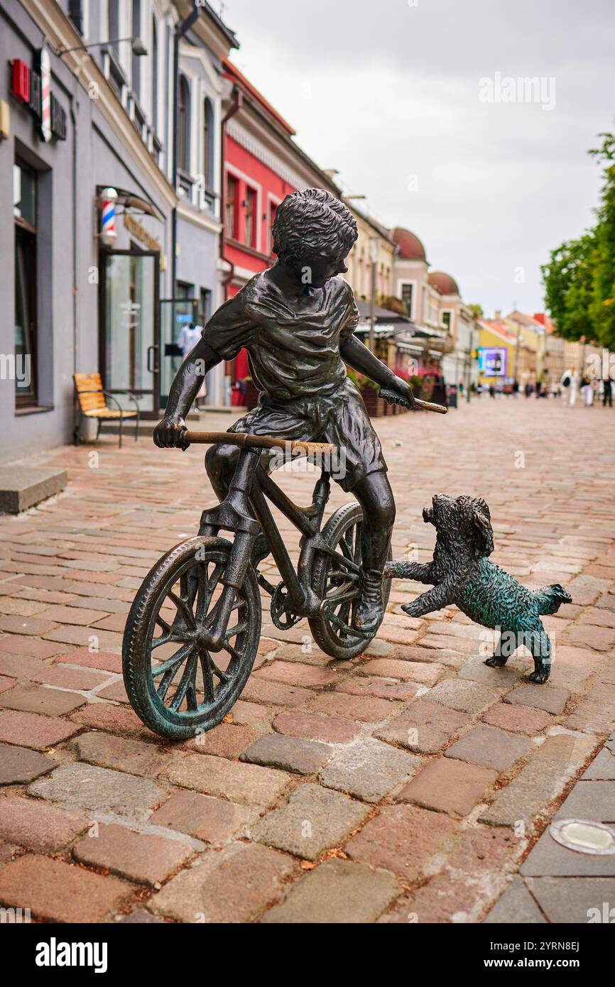 A bronze statue of a boy riding a bicycle with a playful dog at his ...