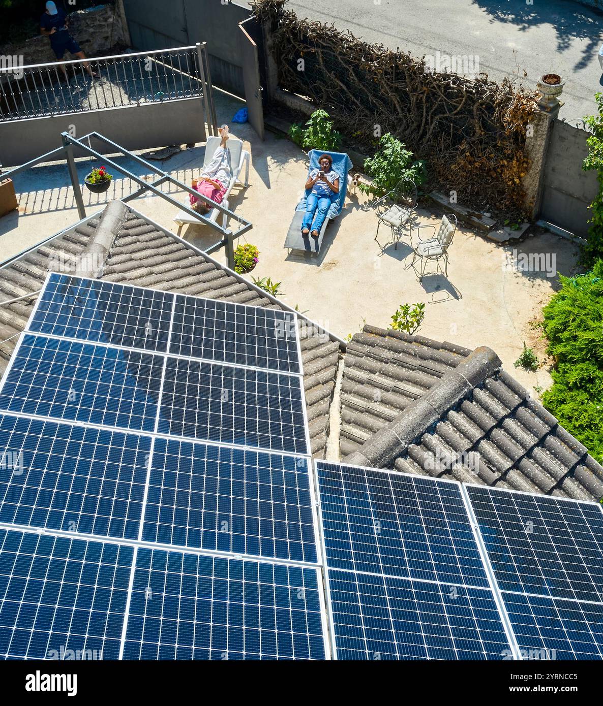 Aerial view of two women sunbathing in a backyard with solar panels ...