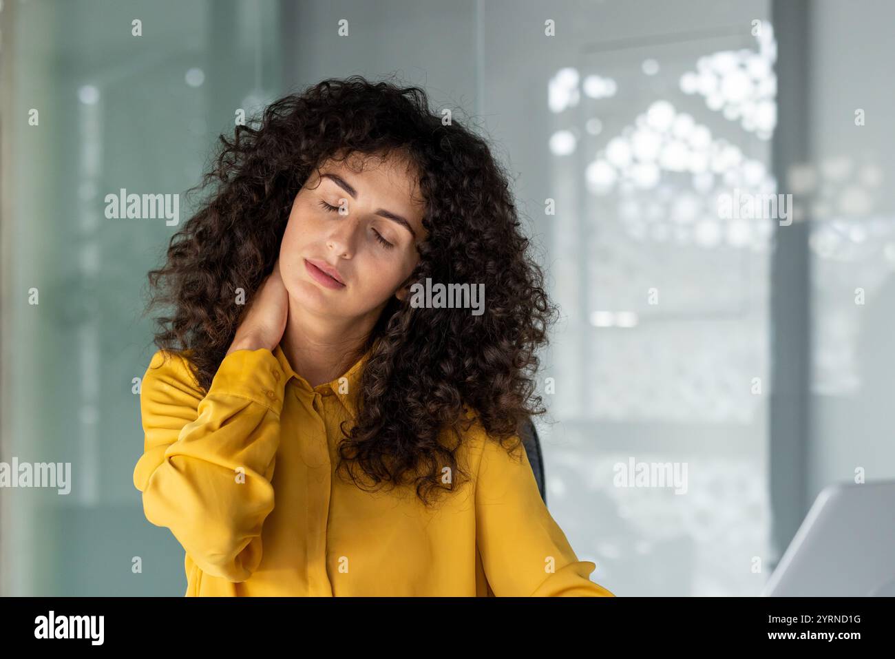 A woman in an office setting is experiencing neck pain, possibly due to ...